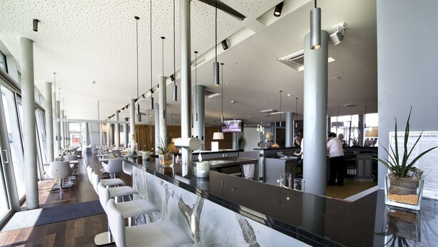 Uma área de bar moderna com bancada de mármore, banquetas brancas e uma janela ampla que proporciona iluminação natural.