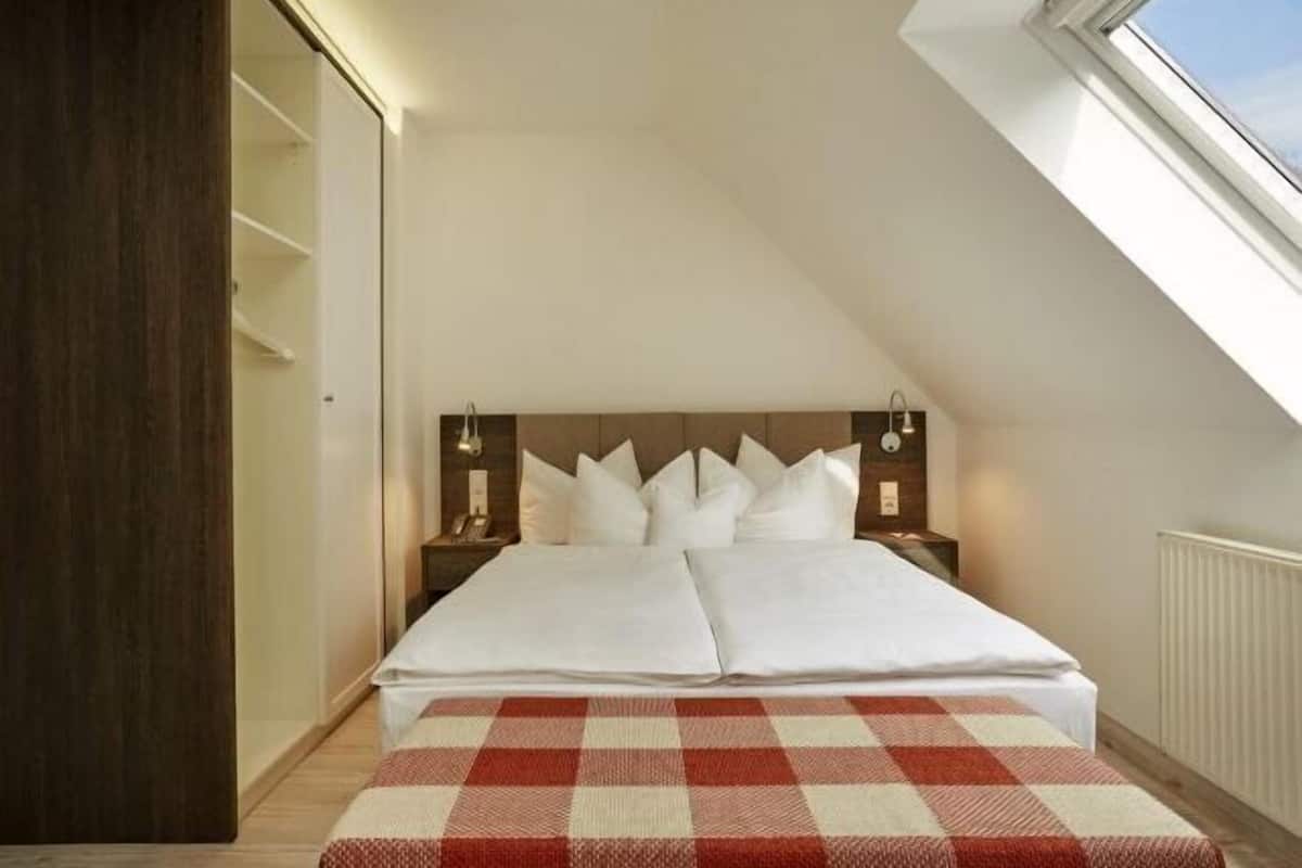 Quarto com uma cama grande, manta xadrez, claraboia e guarda-roupa.