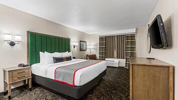 Quarto de hotel com uma cama grande, uma escrivaninha, uma cadeira, uma televisão e uma mesinha.