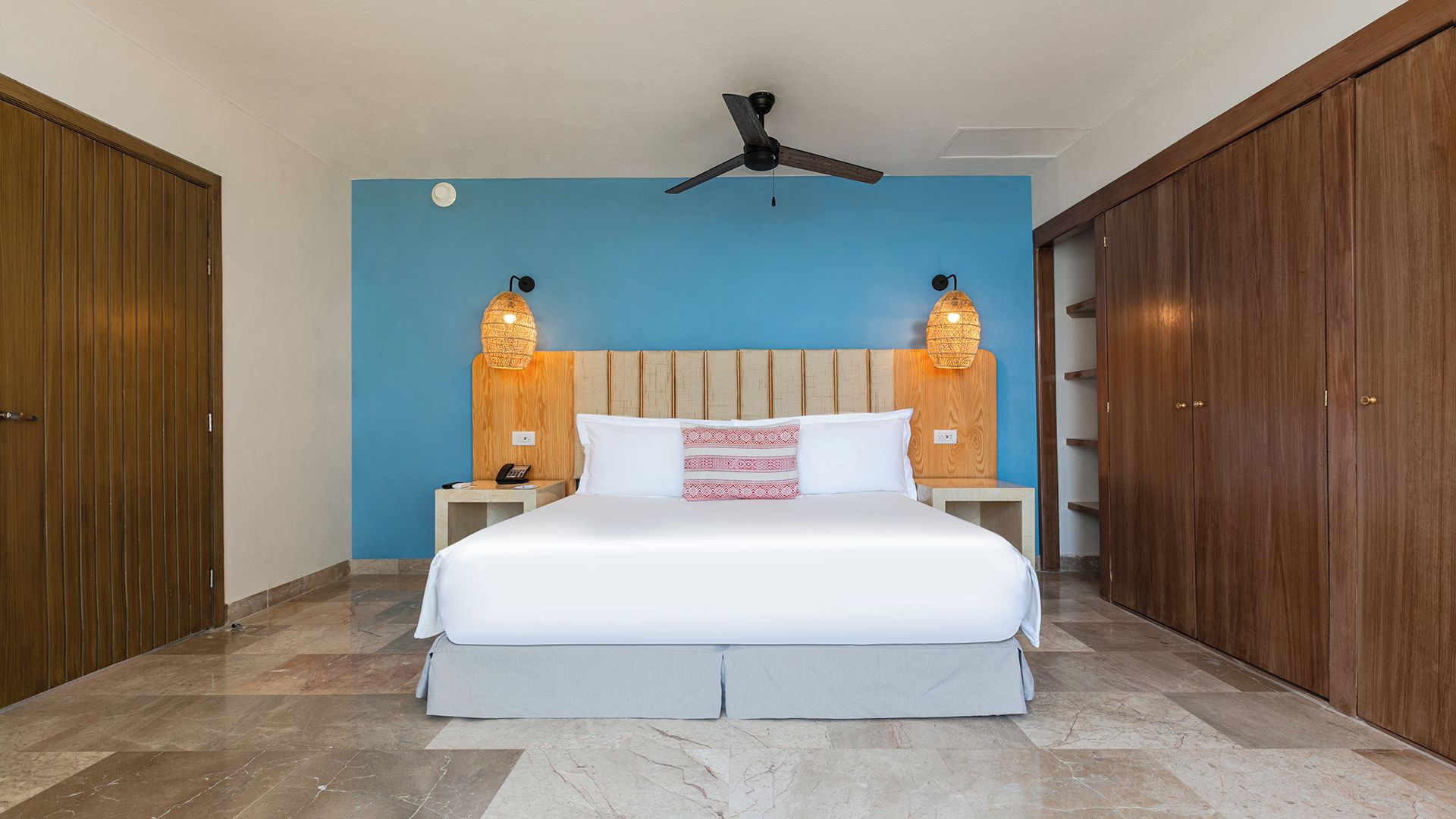 Quarto de hotel com cama, ventoinha no teto, abajures e guarda-roupa.