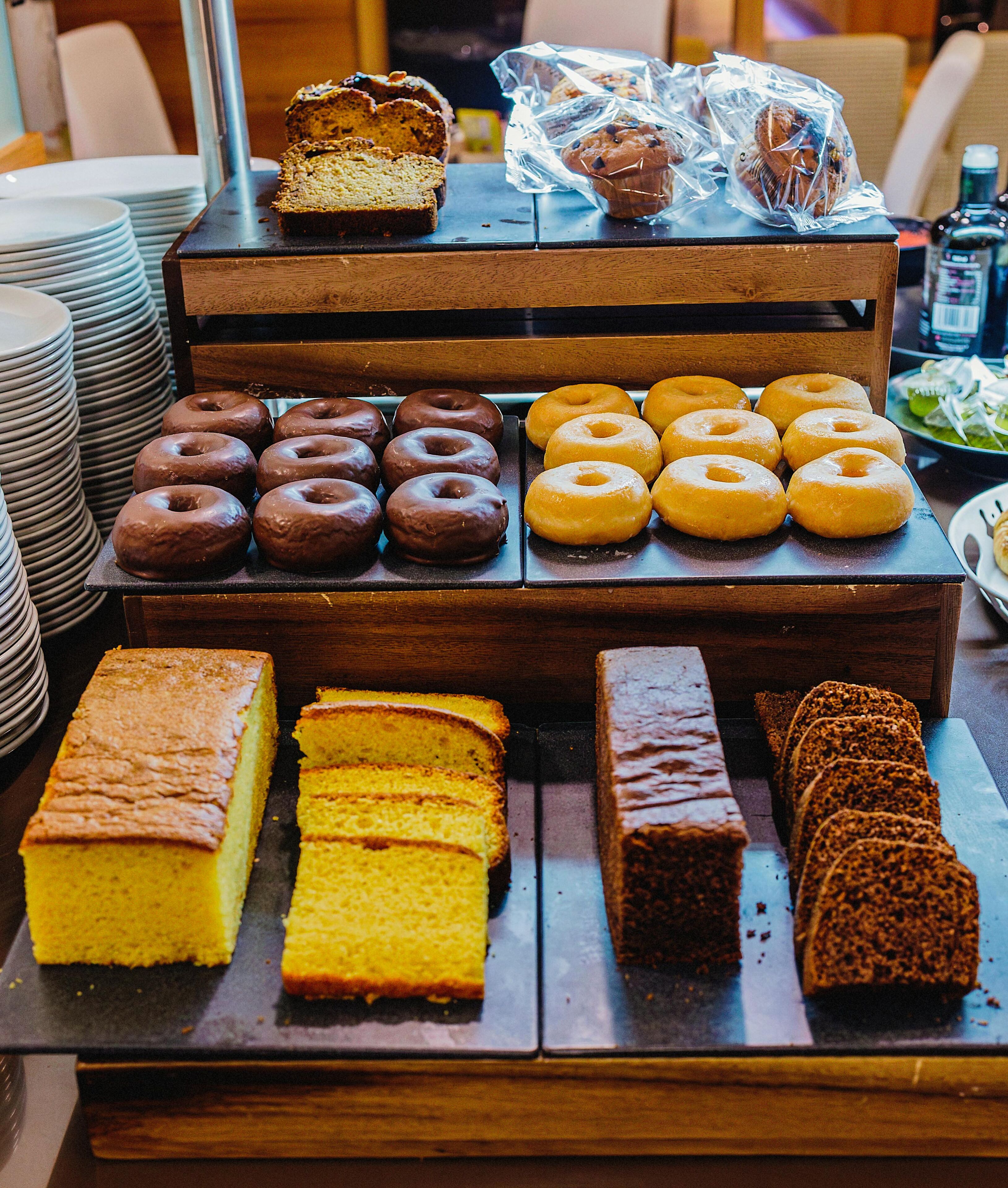 Exposição de diversos produtos de pastelaria, incluindo donuts, muffins e bolos.