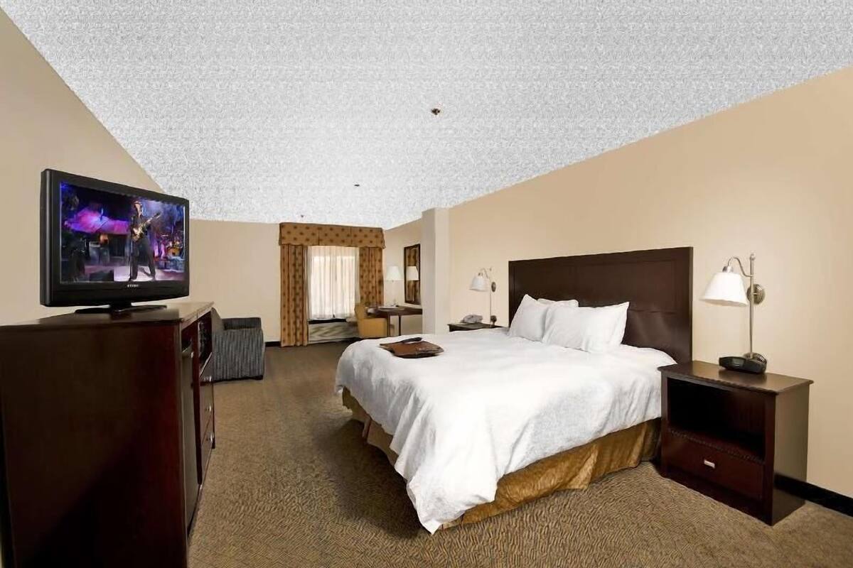 Quarto de hotel com cama, televisão, escrivaninha e cadeira.