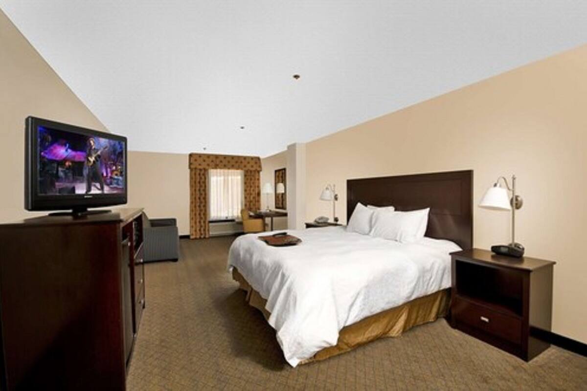Quarto de hotel com cama, televisão, secretária e uma cadeira.