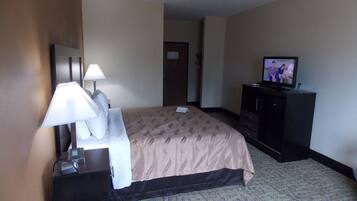 Quarto de hotel com cama, escrivaninha com luminária, televisão e guarda-roupa.