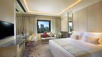 Quarto de hotel com uma cama grande, televisão, escrivaninha e vista para o horizonte urbano pela janela.