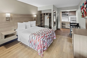 Quarto de hotel com cama, mesas de cabeceira, guarda-roupa, escrivaninha e cozinha compacta.