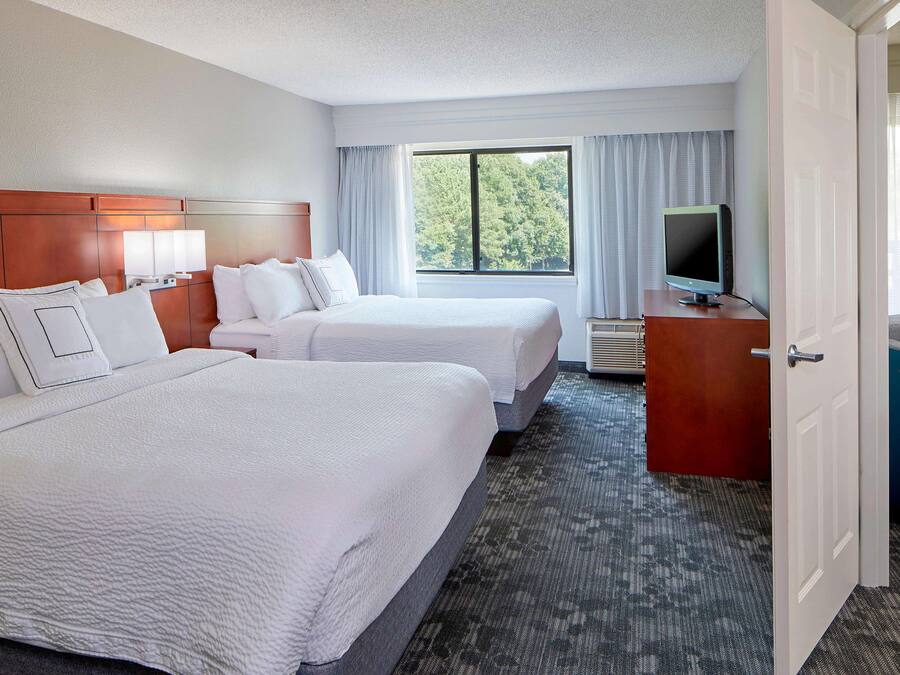 Quarto de hotel com duas camas, televisão e janela com cortinas.