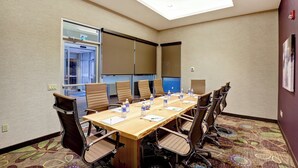 Sala de conferência com uma mesa comprida, cadeiras e porta de vidro que dá para o exterior.