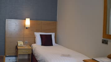 Quarto de hotel com cama, mesa de cabeceira com telefone, luminária na parede e espelho.