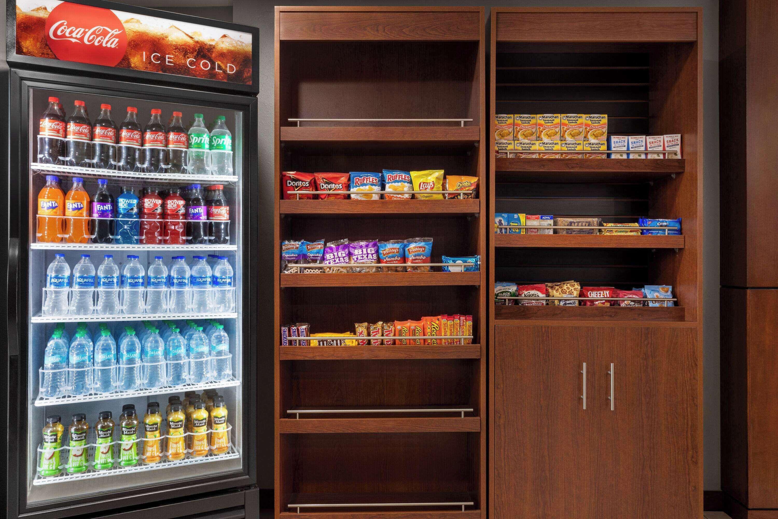 Máquina de vendas com diversas bebidas e lanches, e prateleiras de madeira adjacentes repletas de produtos embalados.