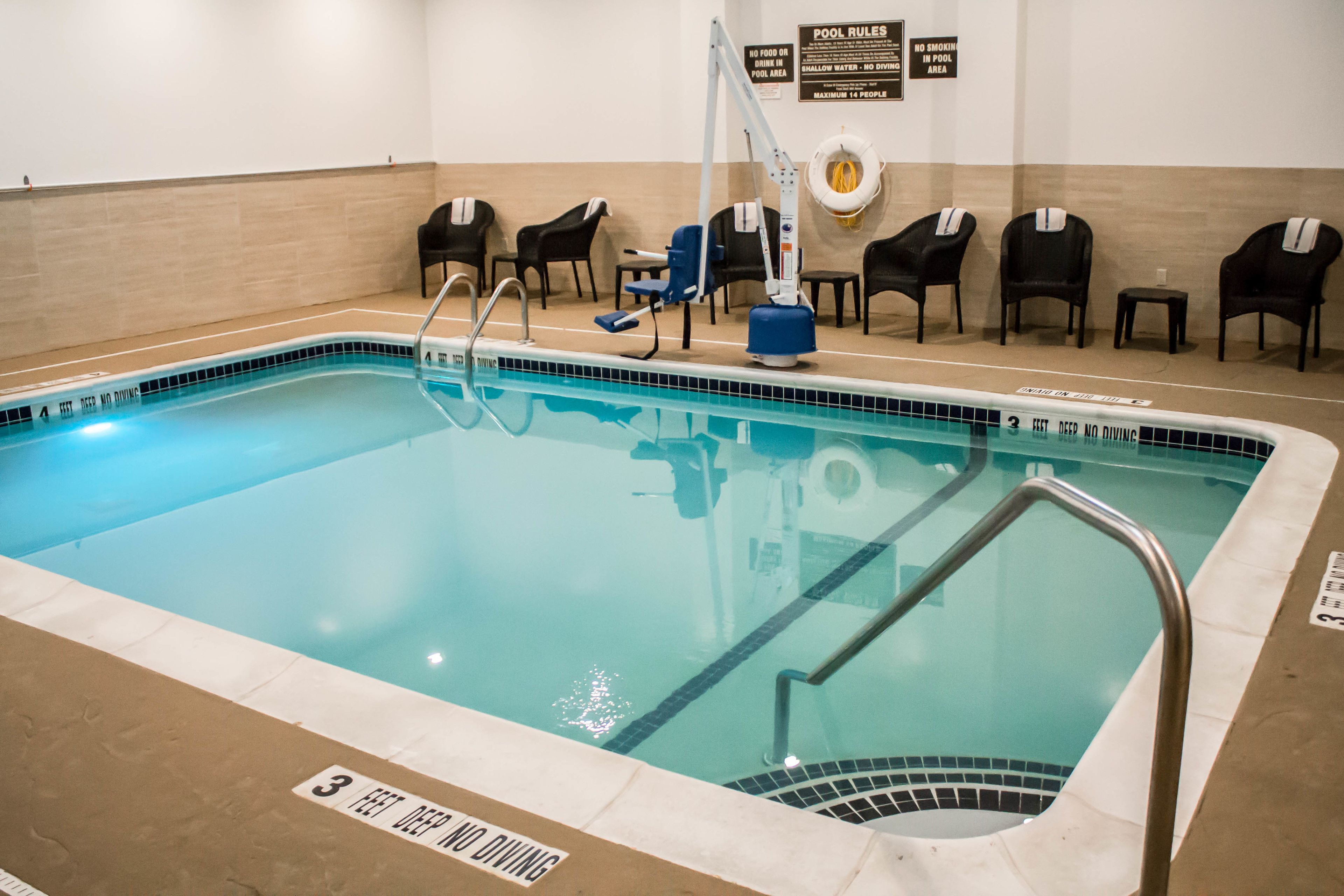 Piscina com trampolim, cadeiras de sol e placas com as regras da piscina.