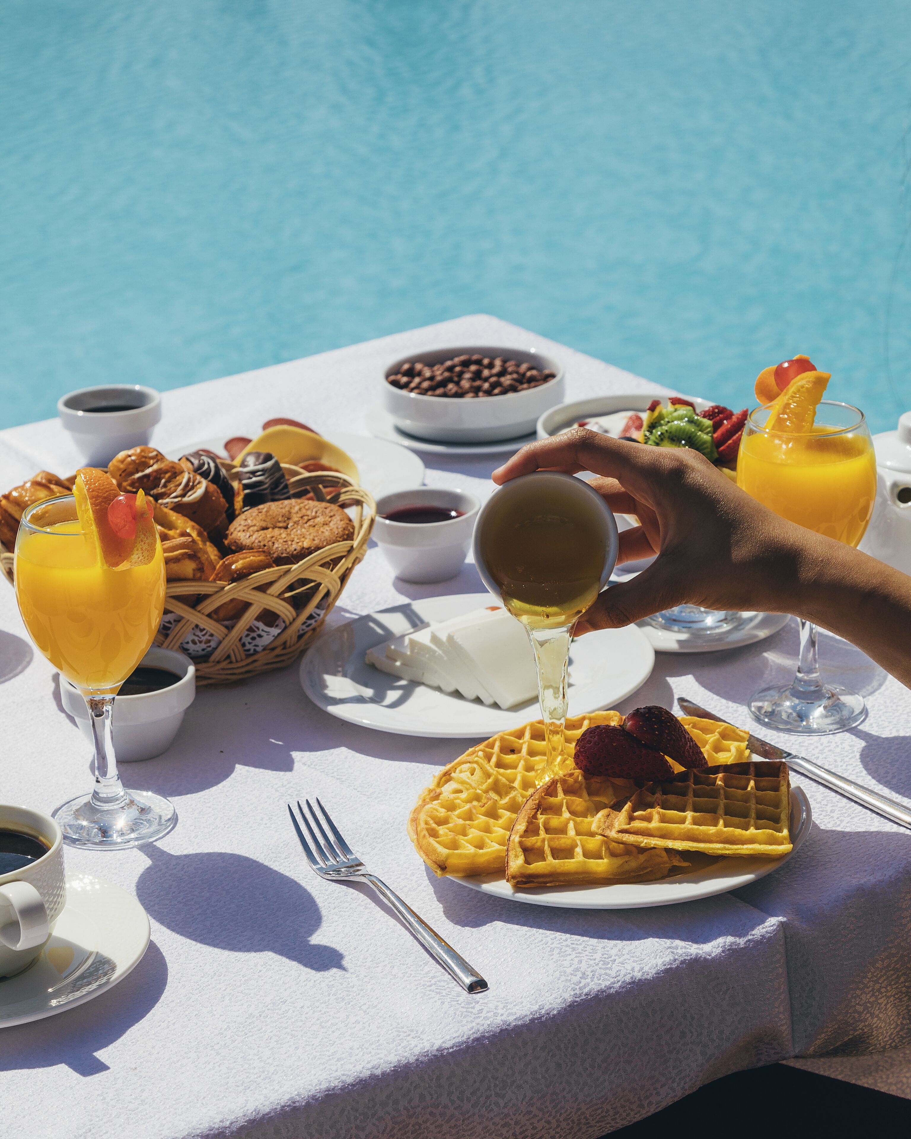 Café da manhã com waffles, café e frutas à beira de uma piscina.