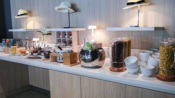 Um buffet de café da manhã com diversos alimentos e acompanhamentos, incluindo potes de compotas, uma cafeteira e um moedor de café.