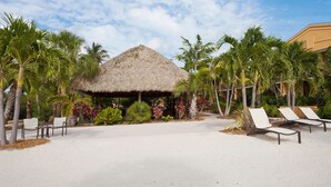 Um resort com estrutura de colmo, palmeiras e espreguiçadeiras numa praia de areia.