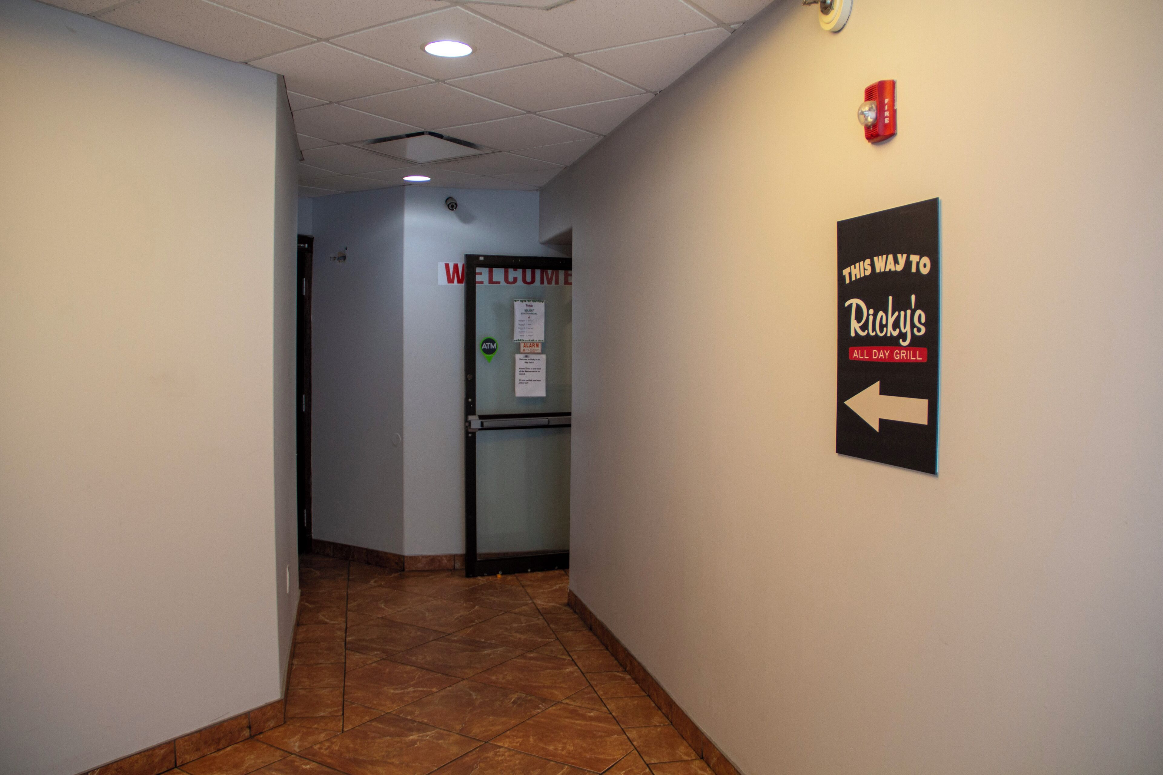 Um corredor com uma placa de boas-vindas, um caixa eletrônico e uma indicação para o Ricky's All Day Grill.