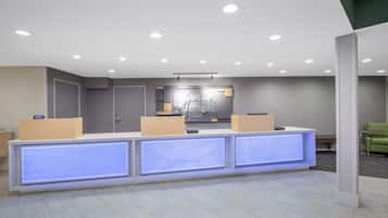 Uma área de recepção com design moderno, destacando um balcão de atendimento com painéis iluminados, uma tela digital e um balcão com a identificação Holiday Inn Express.