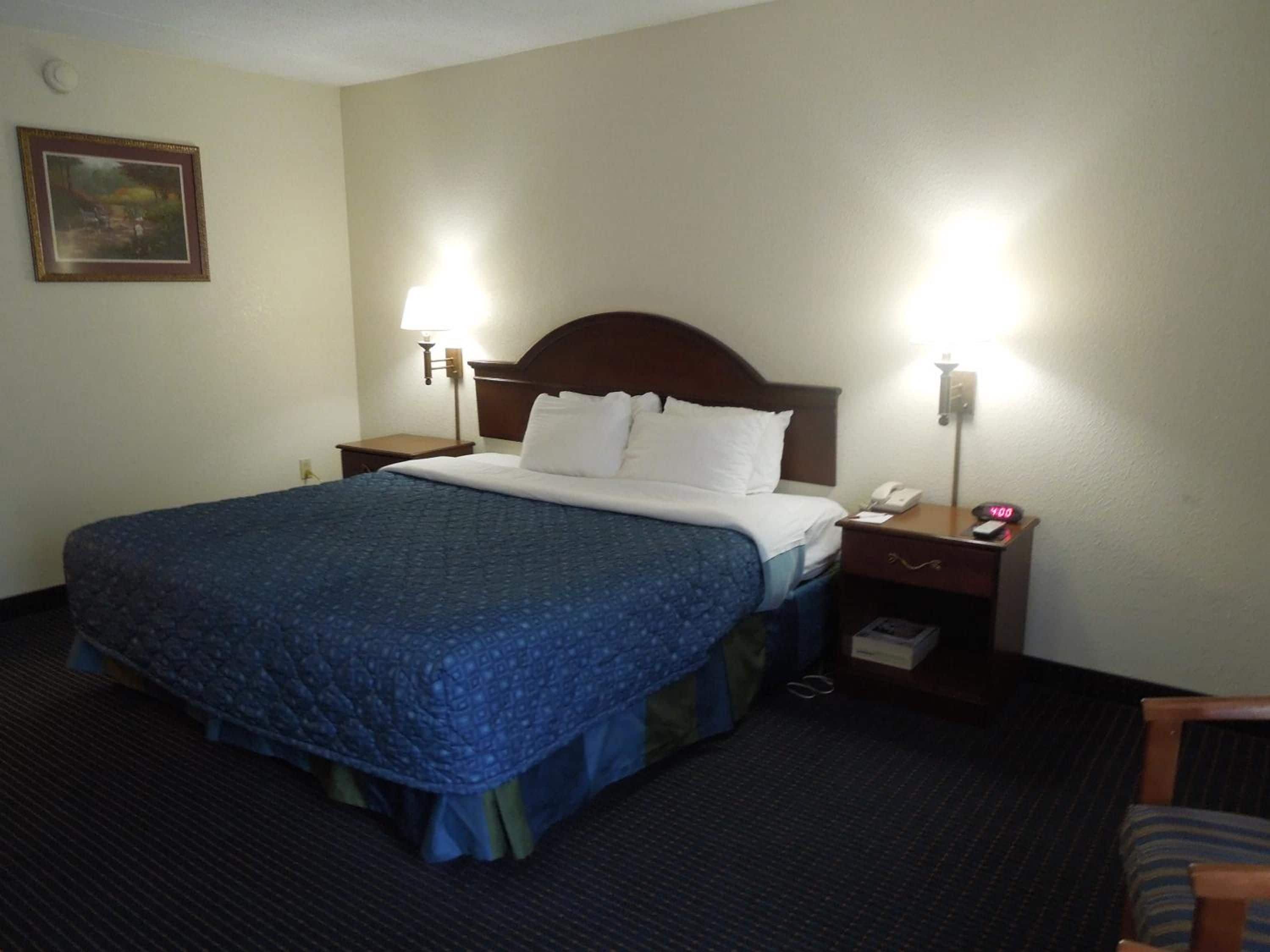 Quarto de hotel com uma cama, duas luminárias de cabeceira, mesa de cabeceira com telefone e quadro na parede.