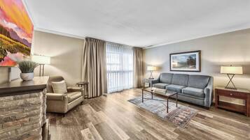 Uma sala de estar com sofá, poltrona, mesa de centro e um quadro na parede.