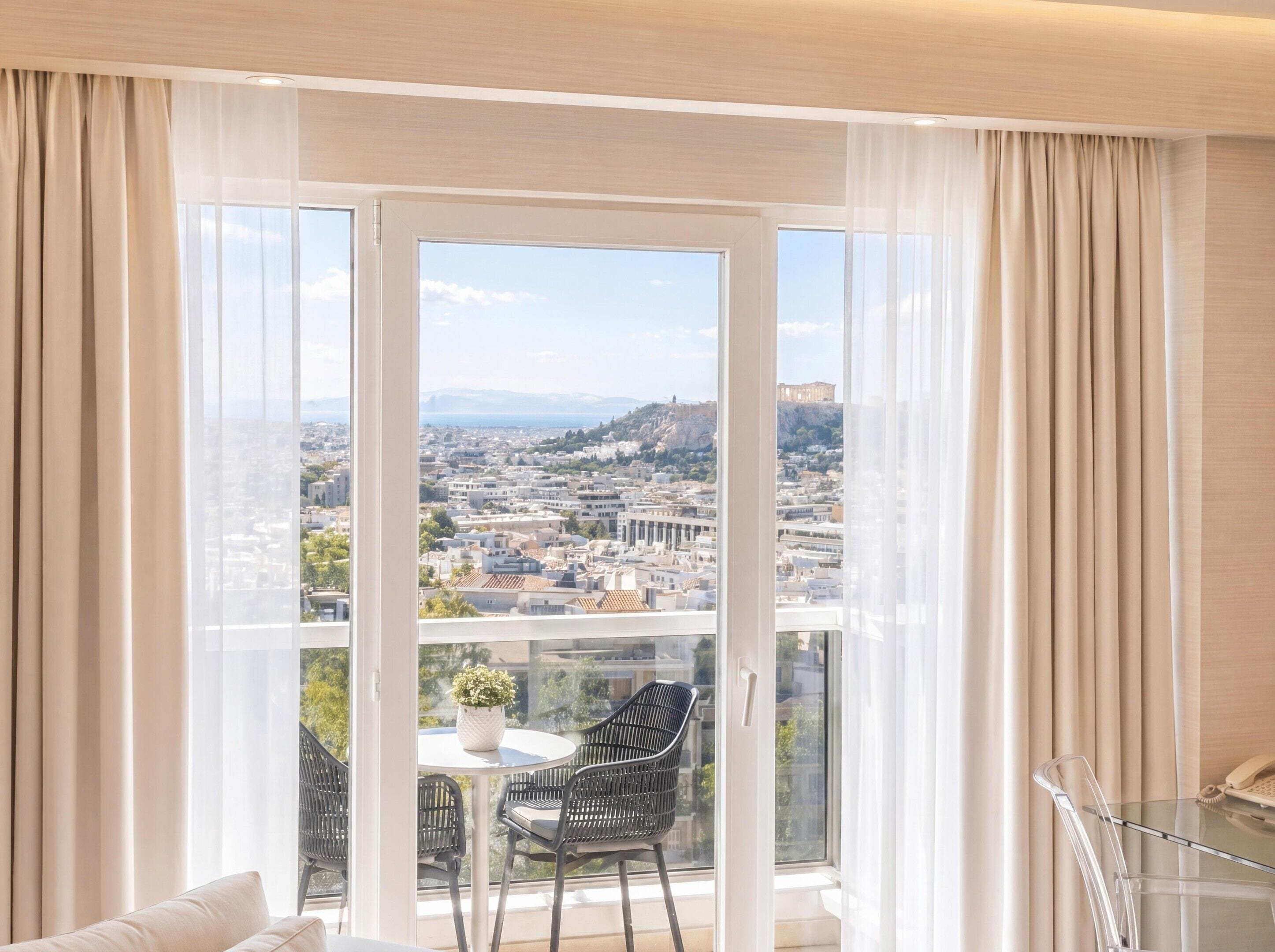 Quarto com varanda, uma mesa com cadeiras e vista para a paisagem urbana.