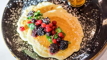 Um prato com panquecas cobertas de frutas vermelhas e hortelã, polvilhado com açúcar de confeiteiro, e uma garrafa de xarope.
