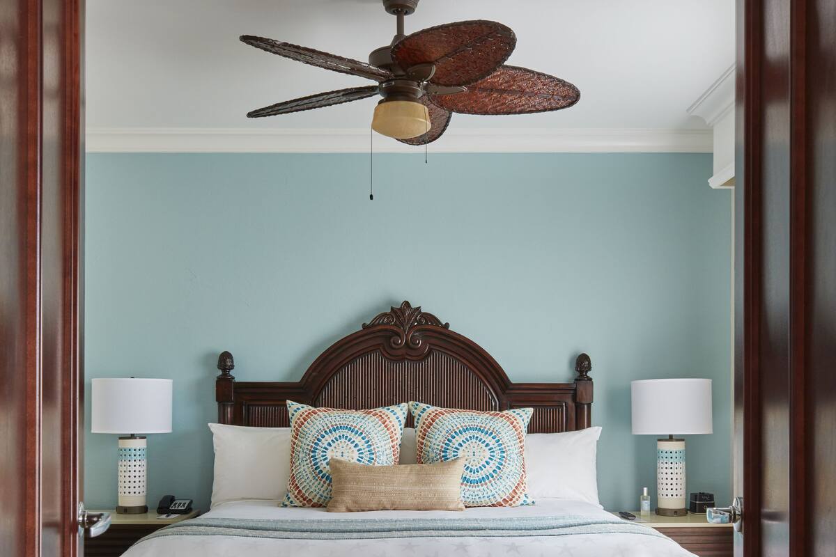 Uma cama grande com cabeceira de madeira, duas luminárias de cabeceira e um ventilador de teto.