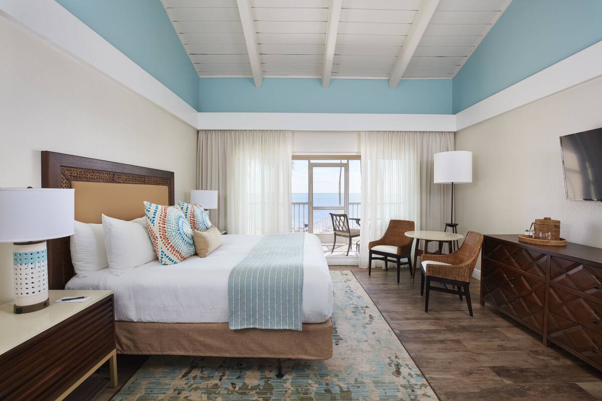 Quarto de hotel com uma cama grande, uma mesa, uma cadeira e vista para o mar.