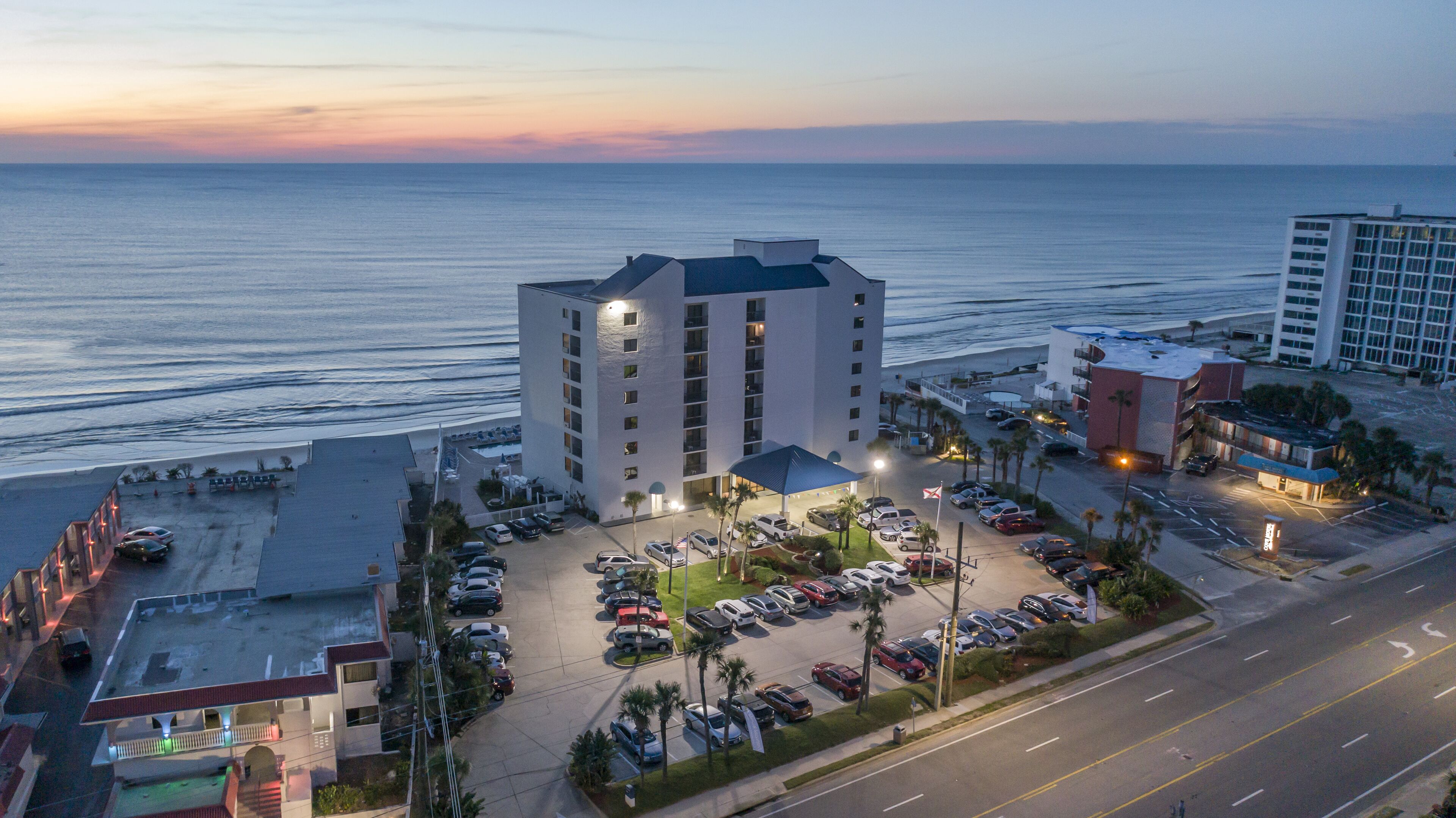 Hotel com estacionamento, vista para a praia e estrada que dá acesso à praia.
