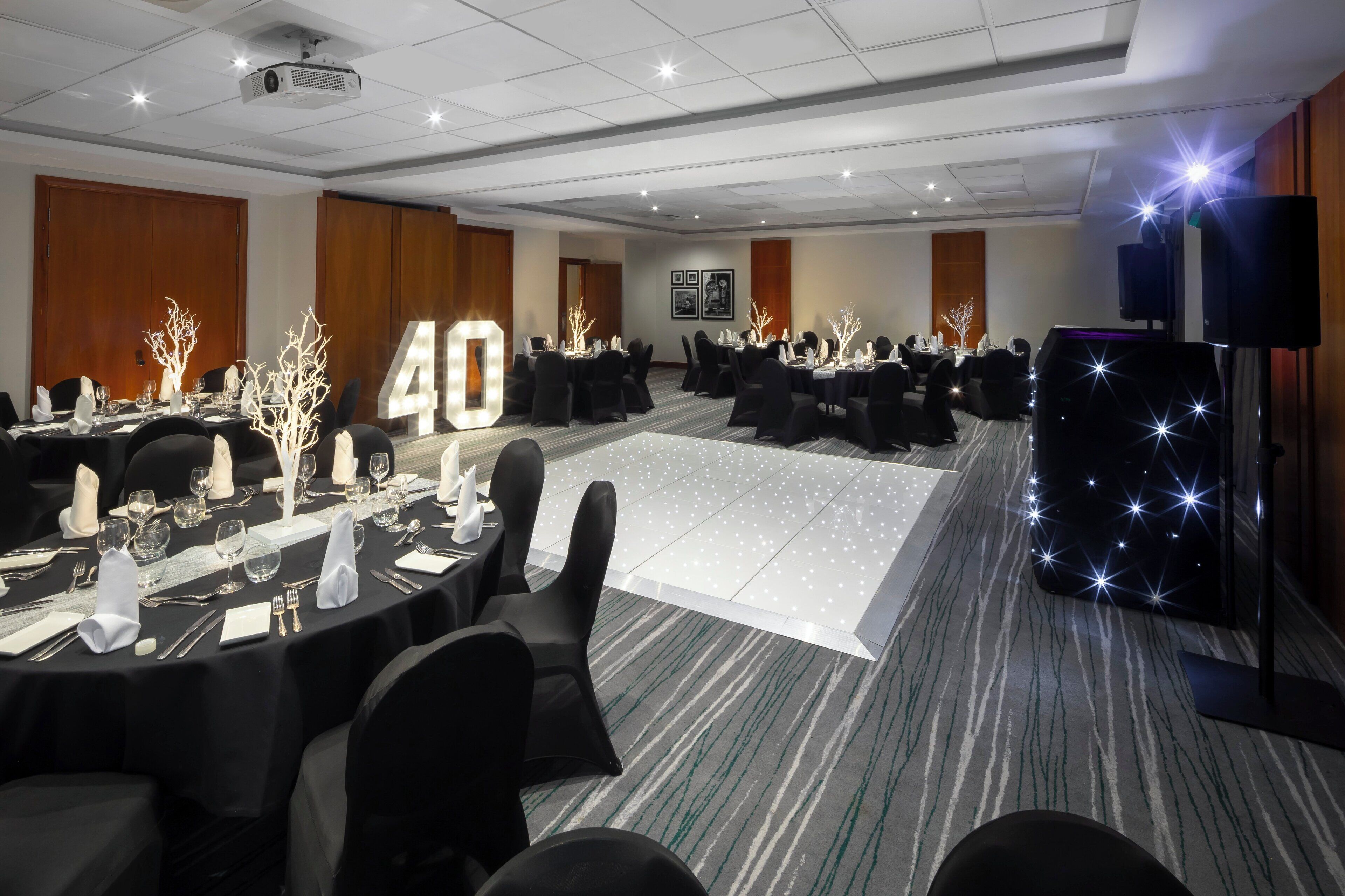 Uma sala de conferências com mesas preparadas para um evento formal, exibindo um número '40' iluminado no chão.
