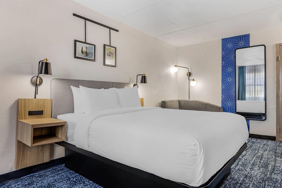 Quarto de hotel com cama, mesas de cabeceira, luminárias fixadas na parede, espelho e parede com padrão azul.