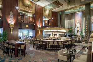 Um saguão de hotel com área de bar, espaços de estar e elementos decorativos.