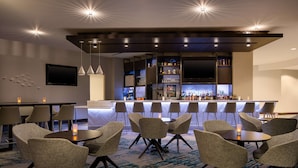 Uma área de bar moderna com um balcão extenso, diversas opções de assento e uma televisão na parede.