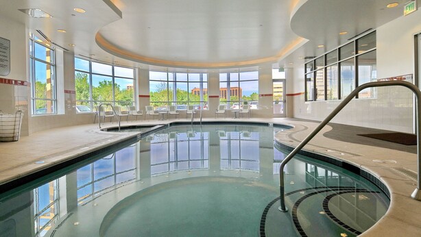 Uma grande piscina interior com paredes de vidro transparente, teto curvo e vista para o exterior.