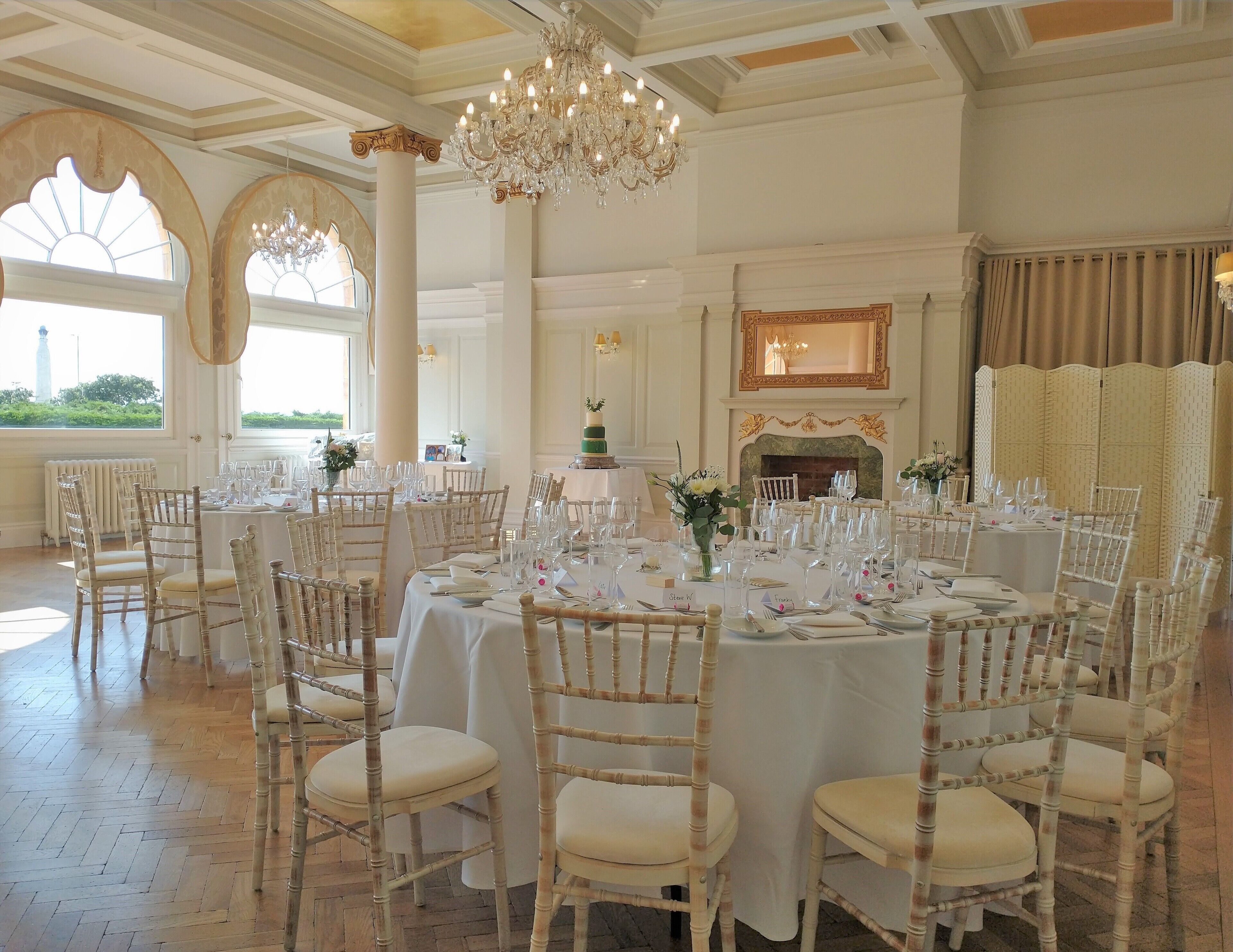 Uma sala de jantar formal com mesas redondas, toalhas de mesa brancas e cadeiras de bambu.