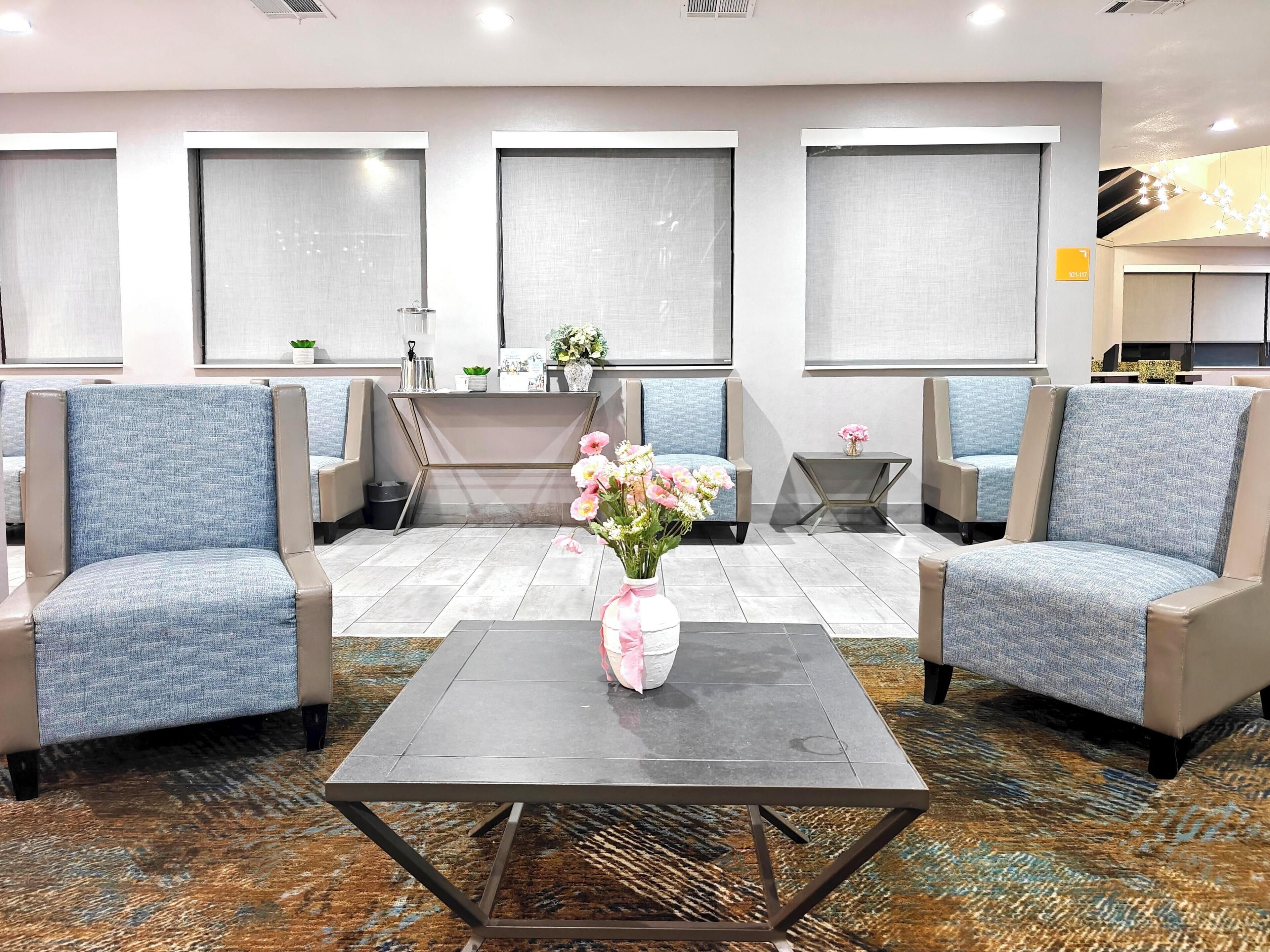 Um saguão de hotel com áreas de estar, um canto para café e um vaso de flores sobre uma mesa.