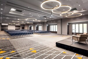Uma sala de conferências ampla, com fileiras de cadeiras, palco e luminárias modernas.