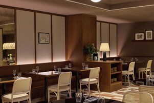 Restaurante com paredes de painel de madeira, uma mesa central com cadeiras e uma pequena mesa lateral com um abajur.