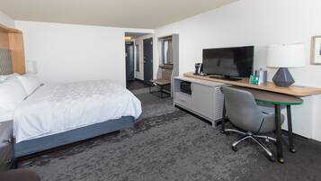 Quarto de hotel com cama, escrivaninha, computador, televisão e uma cadeira.
