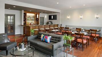 Uma área de bar com adega, assentos com mesas e cadeiras, e um sofá com almofada colorida.