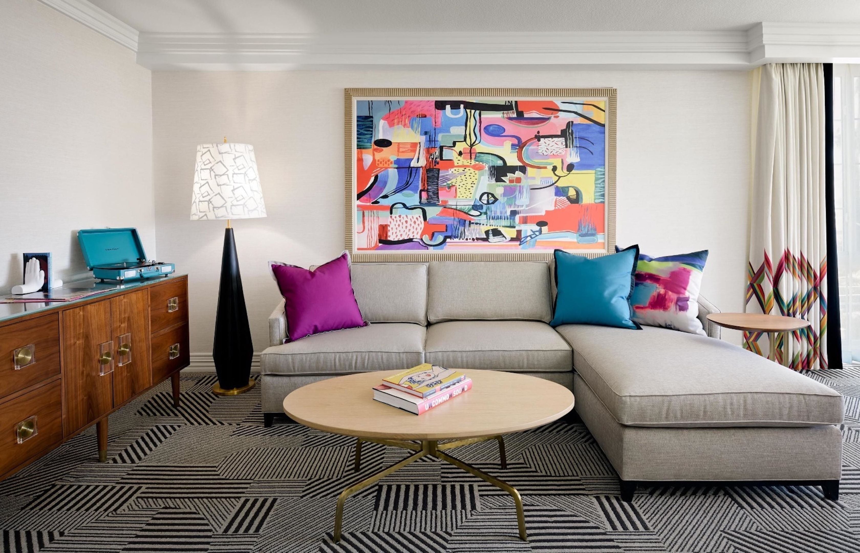 Uma sala de estar moderna com sofá seccional, mesa de centro, abajur, pintura abstrata colorida e tapete estampado.