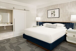 Quarto de hotel com cama, mesas de cabeceira, espelho, quadro emoldurado na parede e tapete estampado.