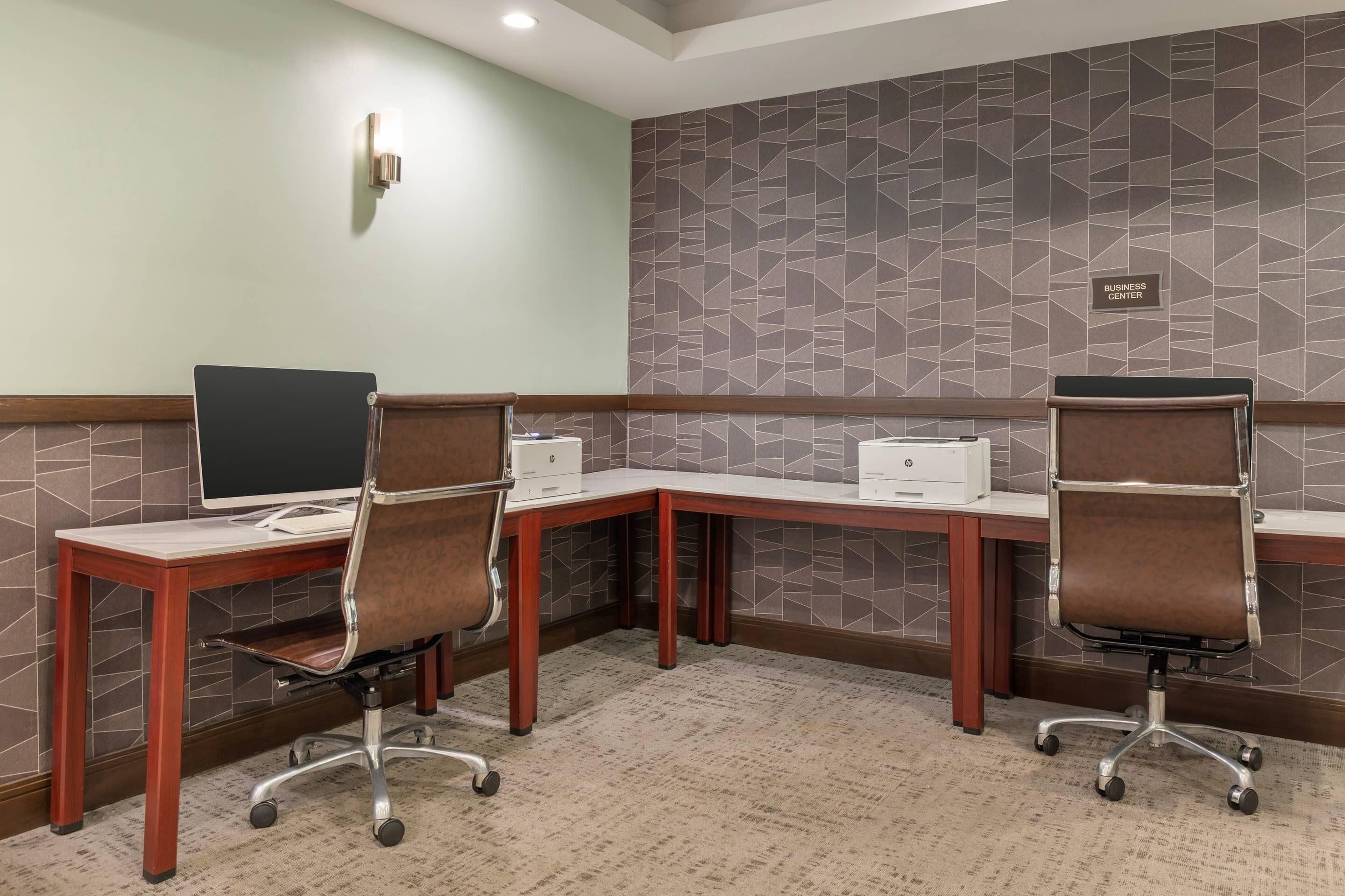 Uma sala de conferências com duas mesas, cadeiras, um computador e uma impressora.