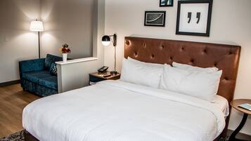 Quarto de hotel com uma cama grande, um sofá azul, uma mesa de cabeceira com abajur e quadros nas paredes.
