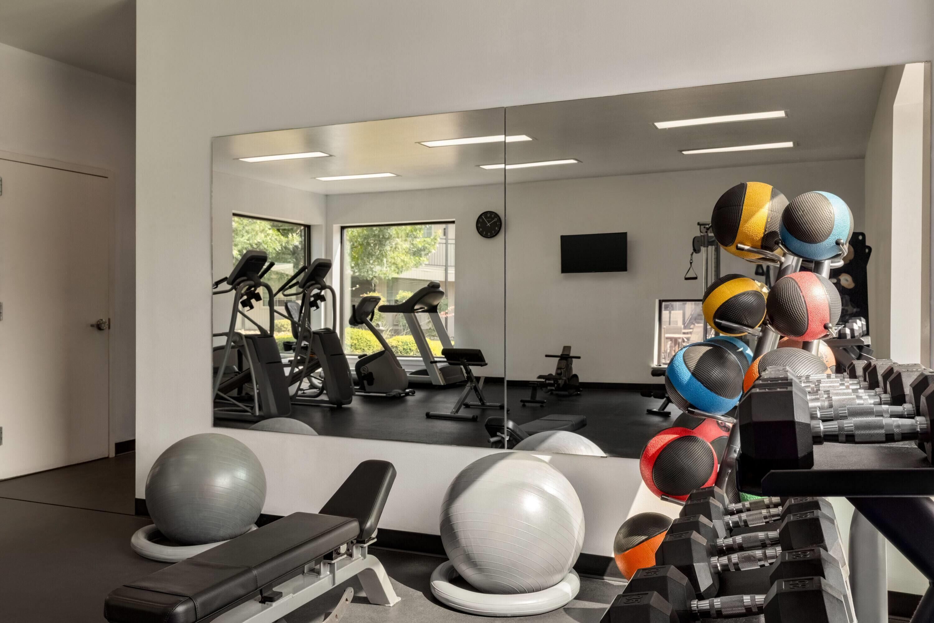 Academia com equipamentos de ginástica, um banco e um espelho grande.