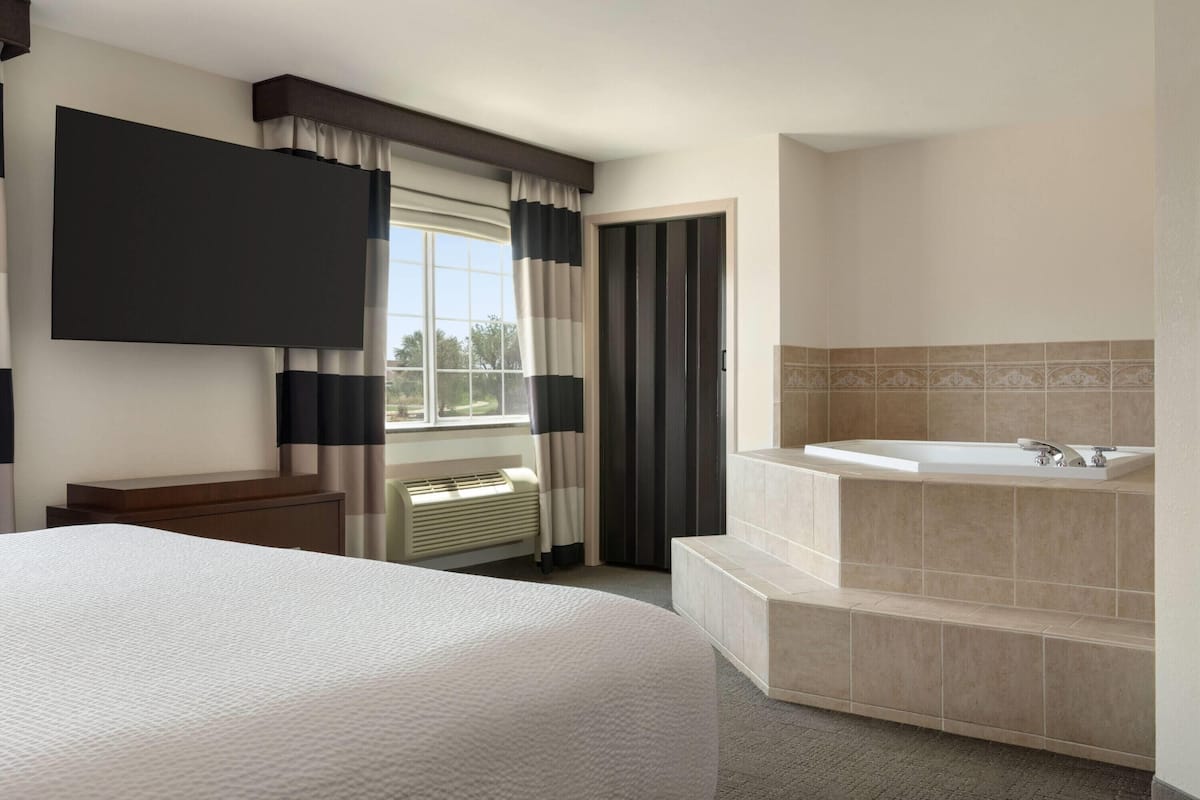 Quarto de hotel com uma cama grande, televisão de tela plana, banheiro com banheira e janela com cortinas.