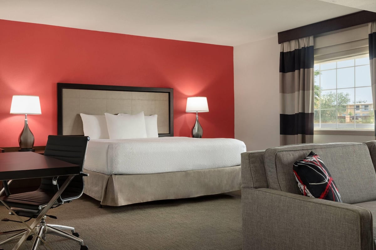 Quarto de hotel com uma cama, duas luminárias de cabeceira, uma escrivaninha com cadeira e um sofá.