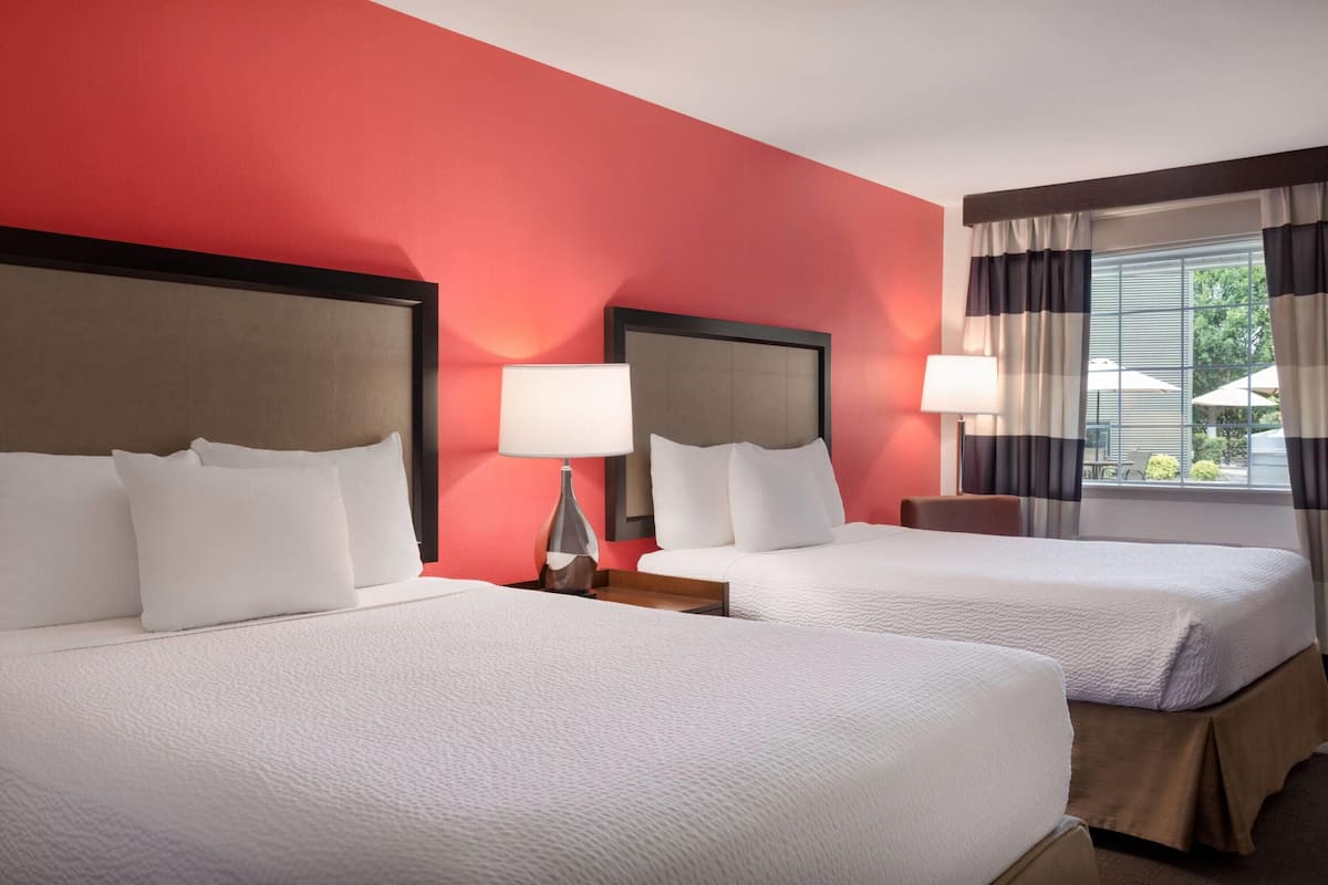 Quarto de hotel com duas camas, uma parede vermelha e uma janela com cortinas.