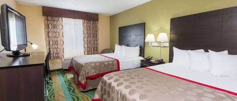 Quarto de hotel com duas camas, uma mesa de trabalho com televisão, uma janela com cortinas estampadas e um tapete padronizado.