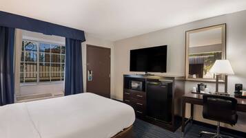 Quarto de hotel com cama, escrivaninha com computador, televisão e espelho.