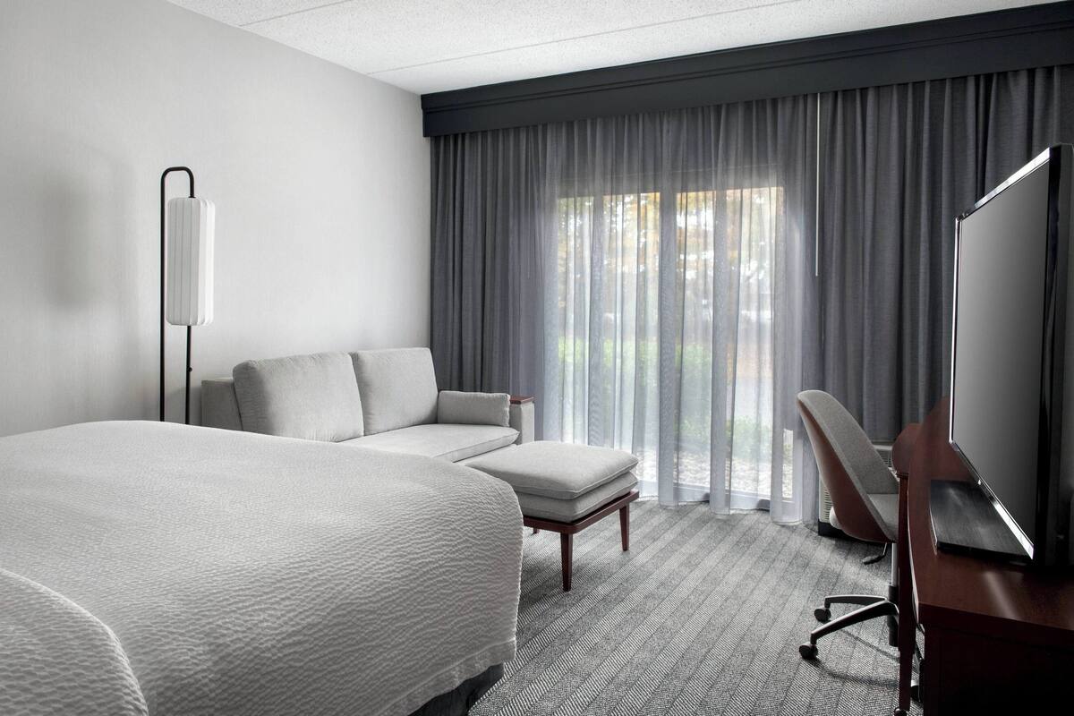Quarto de hotel com uma cama grande, um sofá, uma escrivaninha com um computador e uma cadeira.