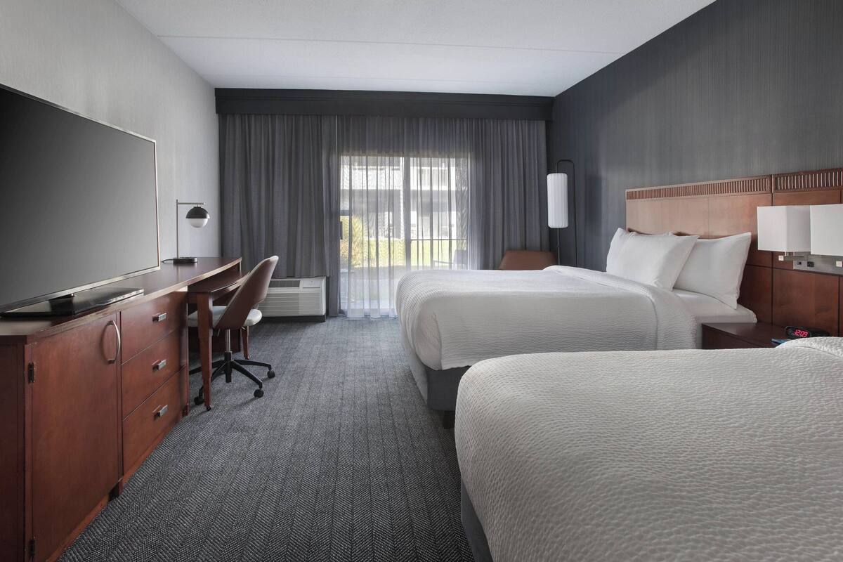 Quarto de hotel com uma cama grande, escrivaninha, cadeira e televisão.